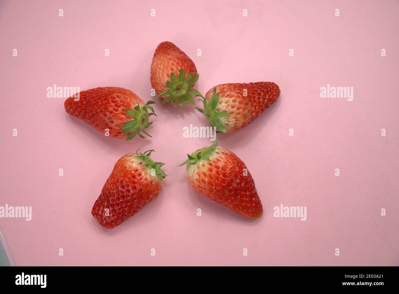 Five organic strawberries arranged in pentagram shape, pink background ...