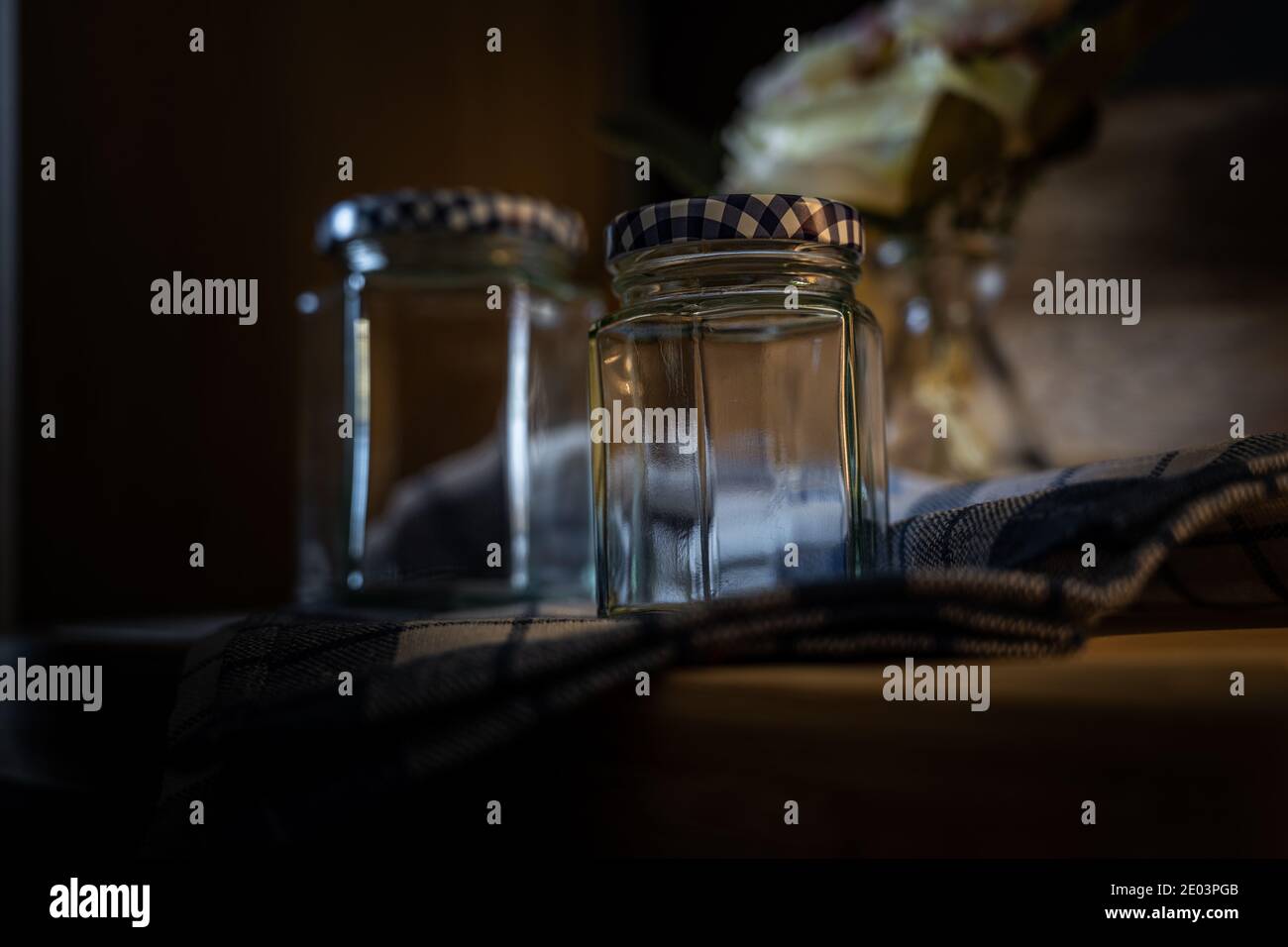 Dark and moody still life of two empty glass jars with blue check ...