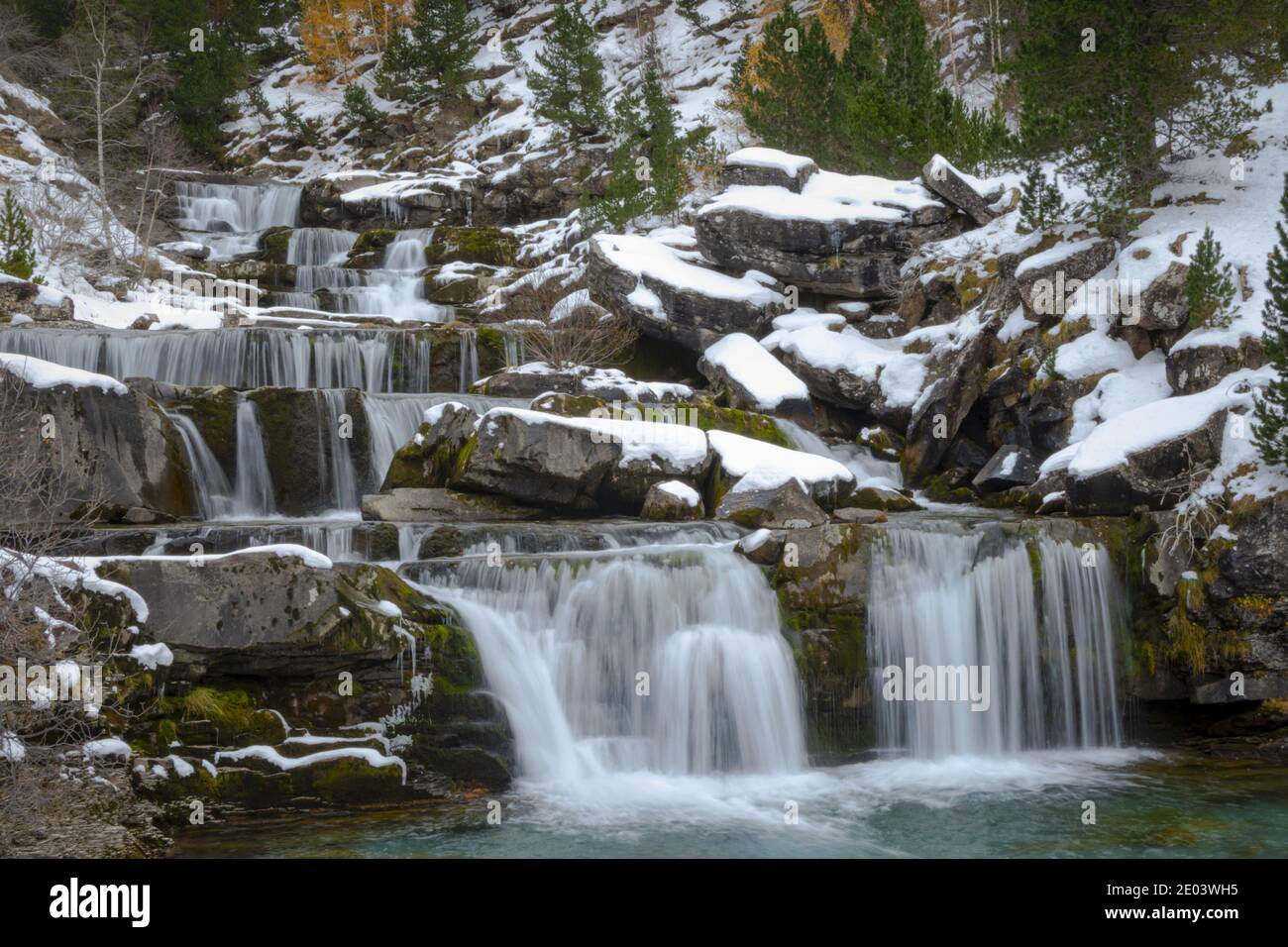 river going through snowy valley in rock waterfalls with snowy trees ...
