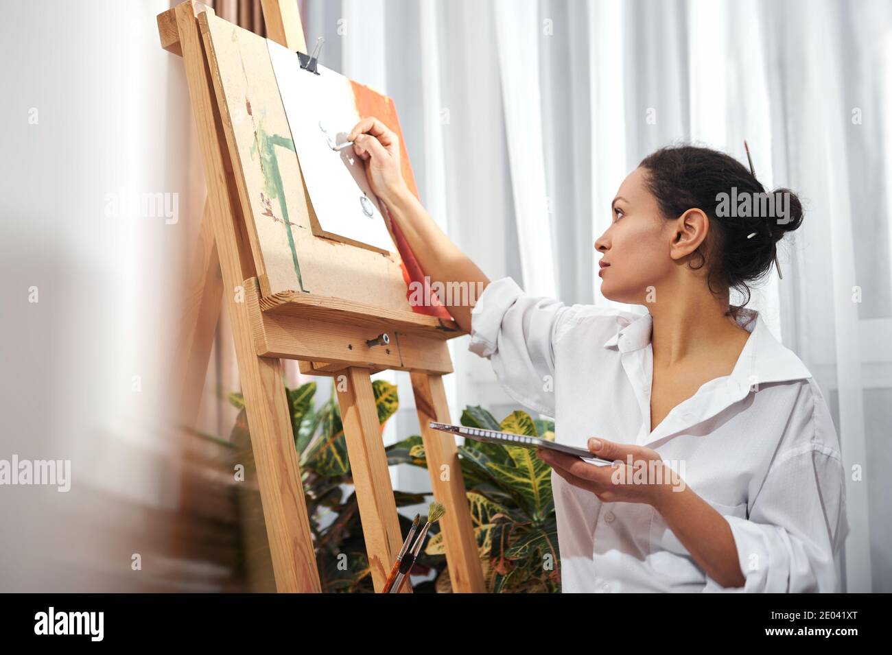 Side view of beautiful brunette painter with gathered hair in a bun and ...