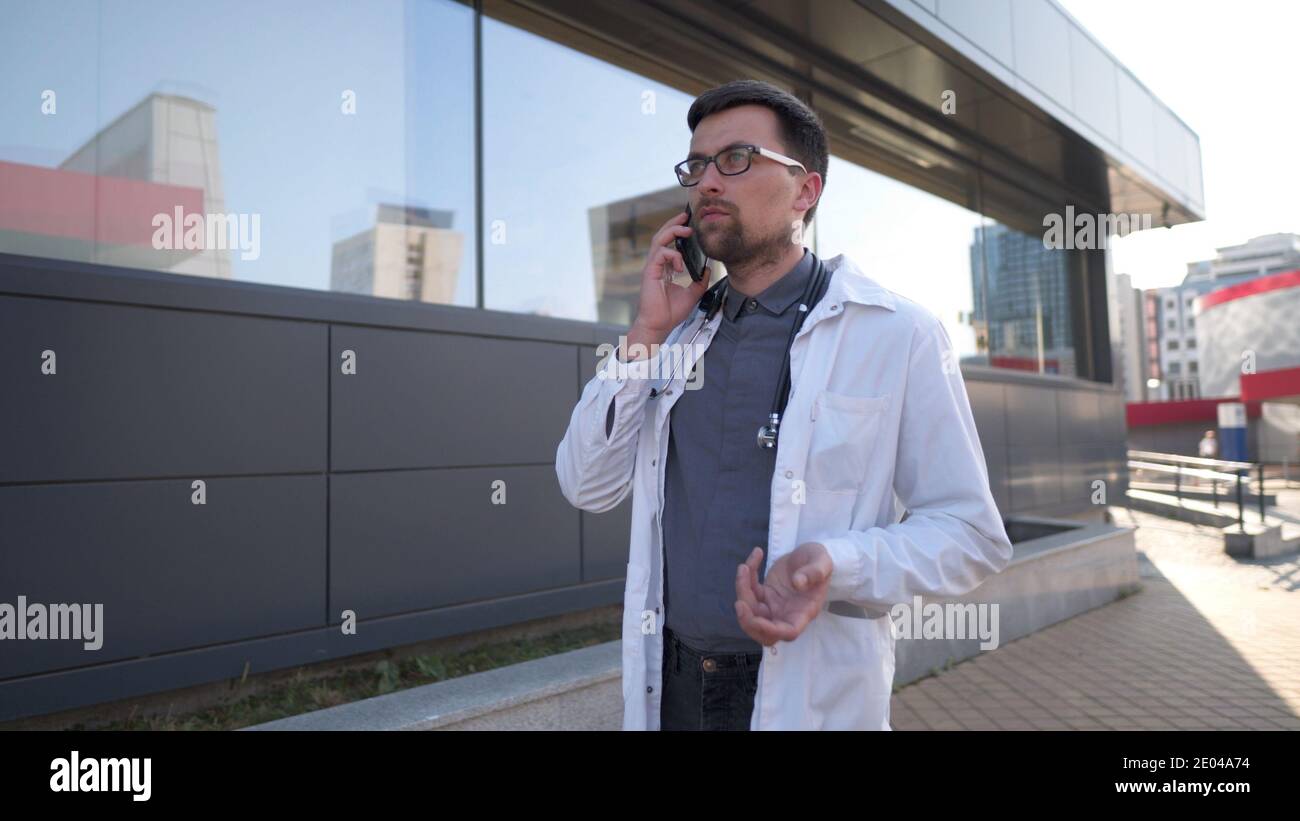 Young Caucasian doctor in white medical coat consults patient on cell ...
