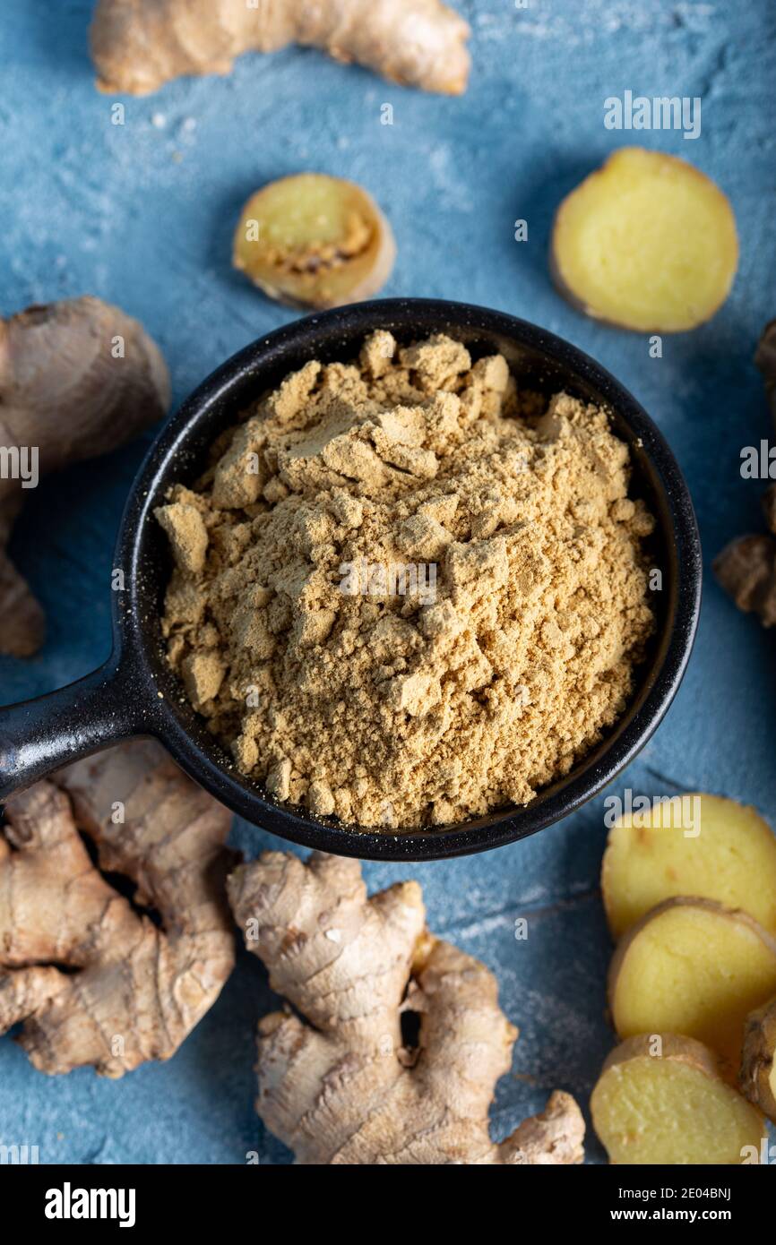 Fresh ginger root and ground ginger spice in black bowl on blue ...