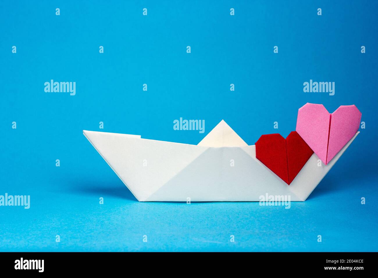 White paper boat and two hearts on a blue background. The theme of ...