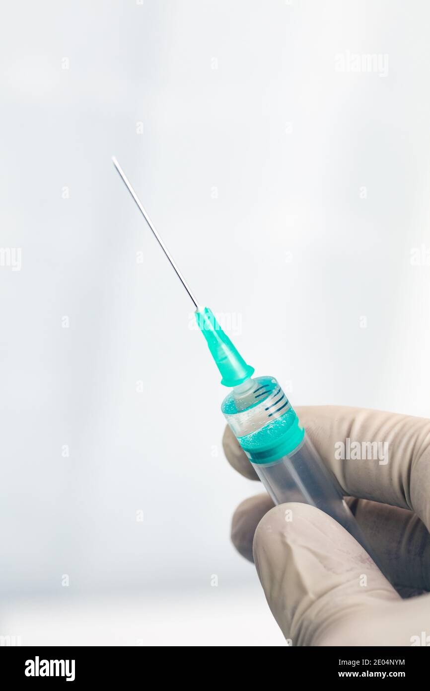 Male hand in white gloves holding a plastic syring with liquid for ...