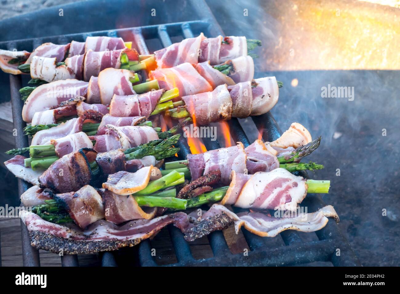 Open Fire cooking asparagus wrapped in bacon, with smoke from the fire ...