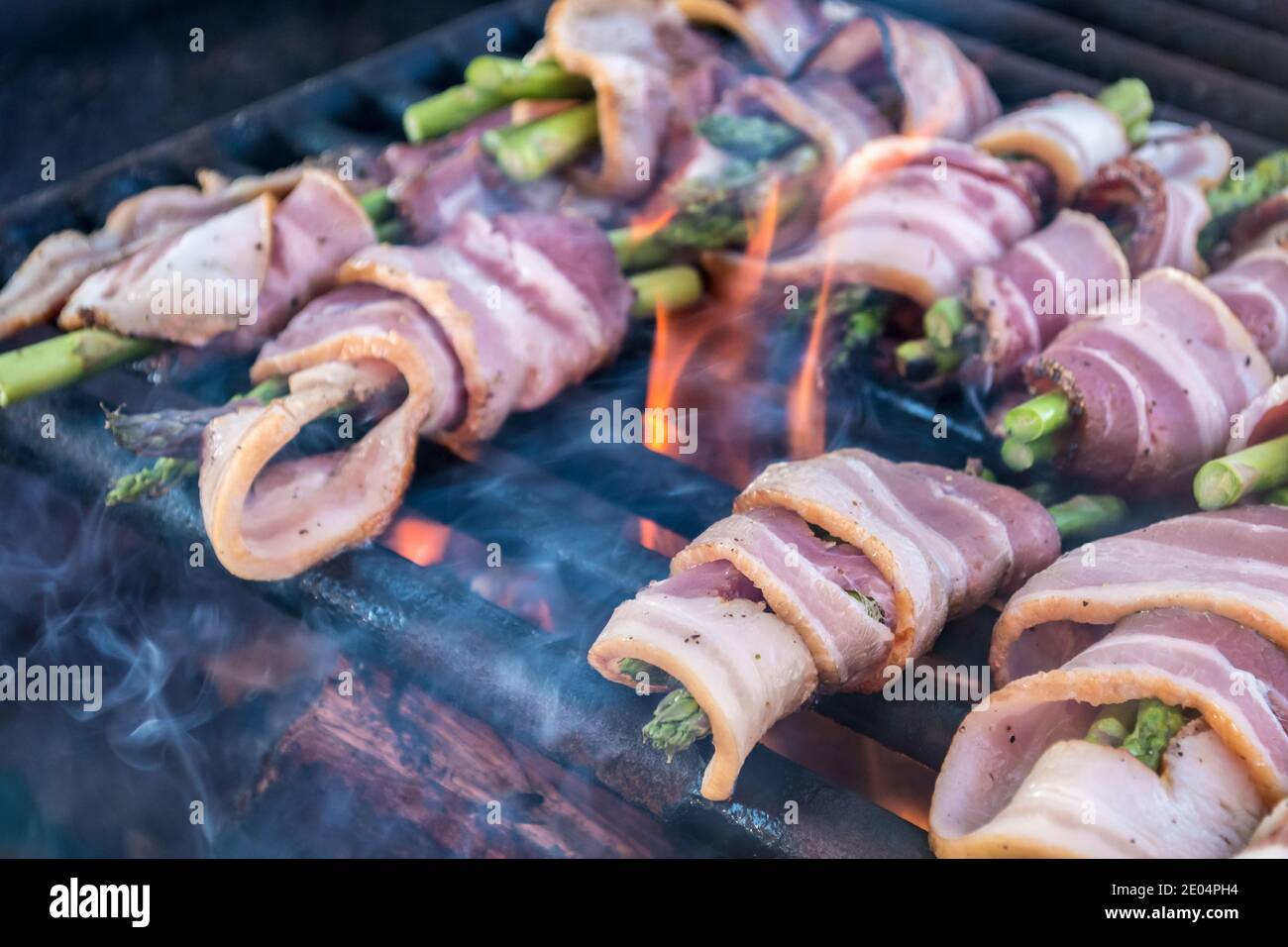 Open Fire cooking asparagus wrapped in bacon, with smoke from the fire ...