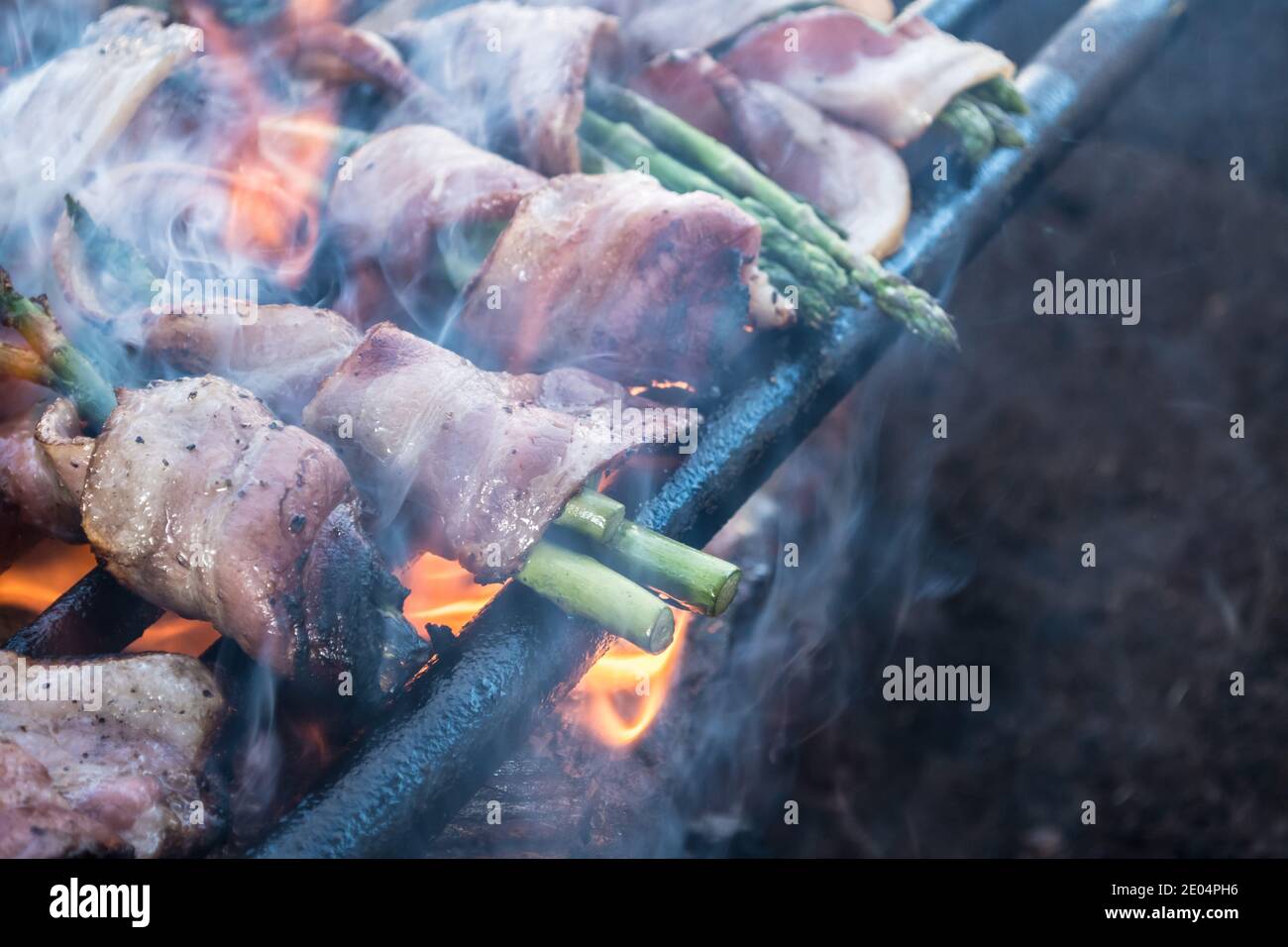 Open Fire cooking asparagus wrapped in bacon, with smoke from the fire ...