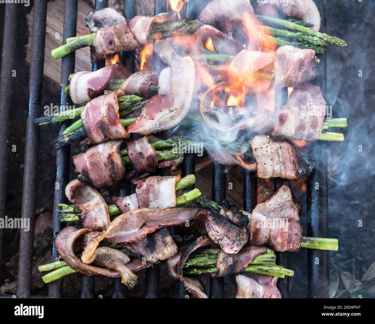 Open Fire cooking asparagus wrapped in bacon, with smoke from the fire ...