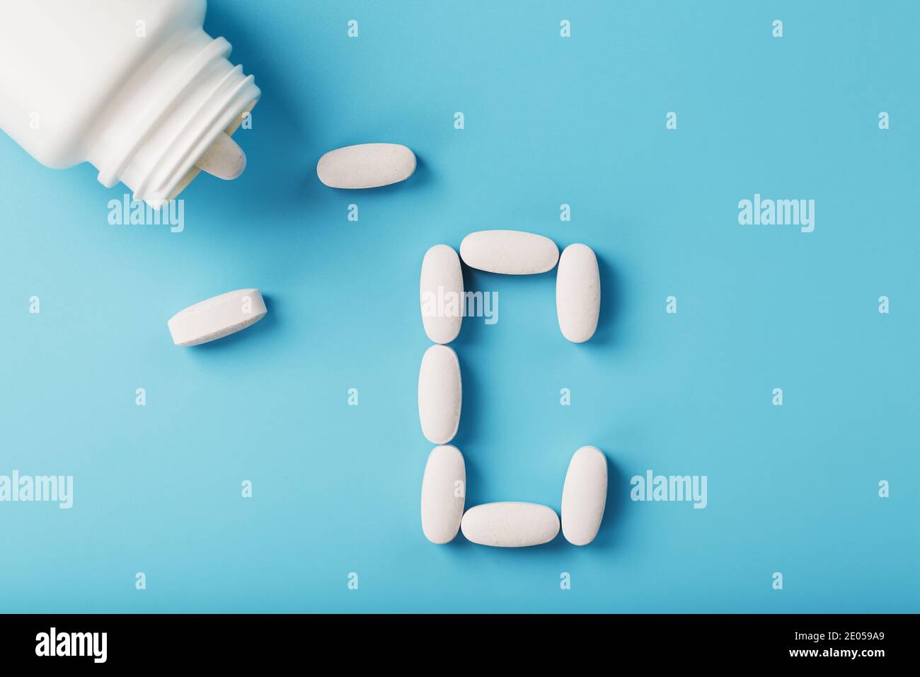 The letter of vitamin C in capsules pour out from the jar on a blue ...