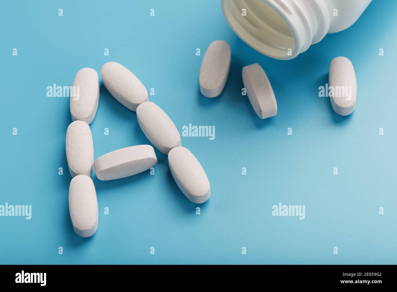Vitamin A pills fell out of a white jar on a blue background. The ...