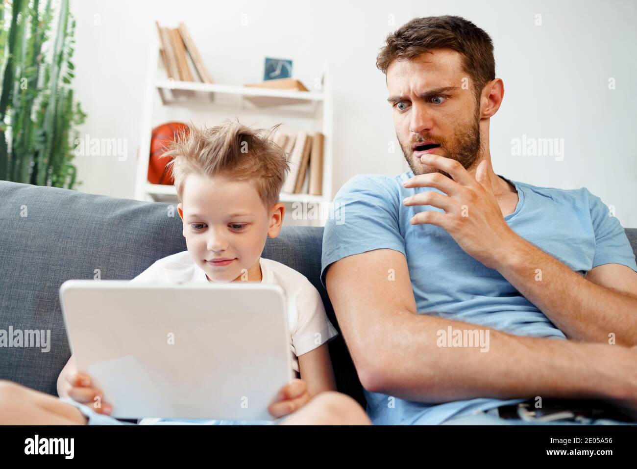Worried father peeking at what his son is watching on digital tablet ...