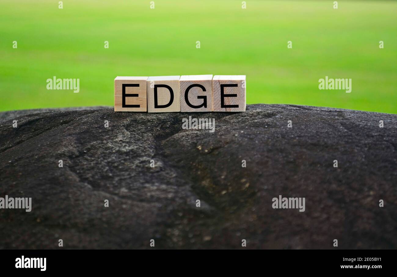 Edge text on wooden cube block on top of big stone with blurred green ...
