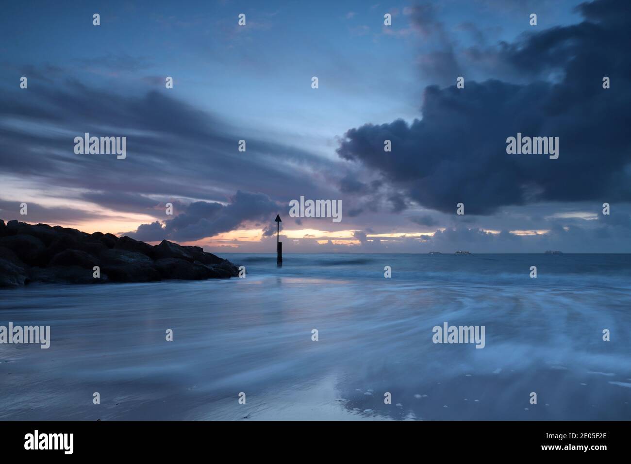 Waves rush towards the camera on Bournemouth beach in a cold, subdued ...