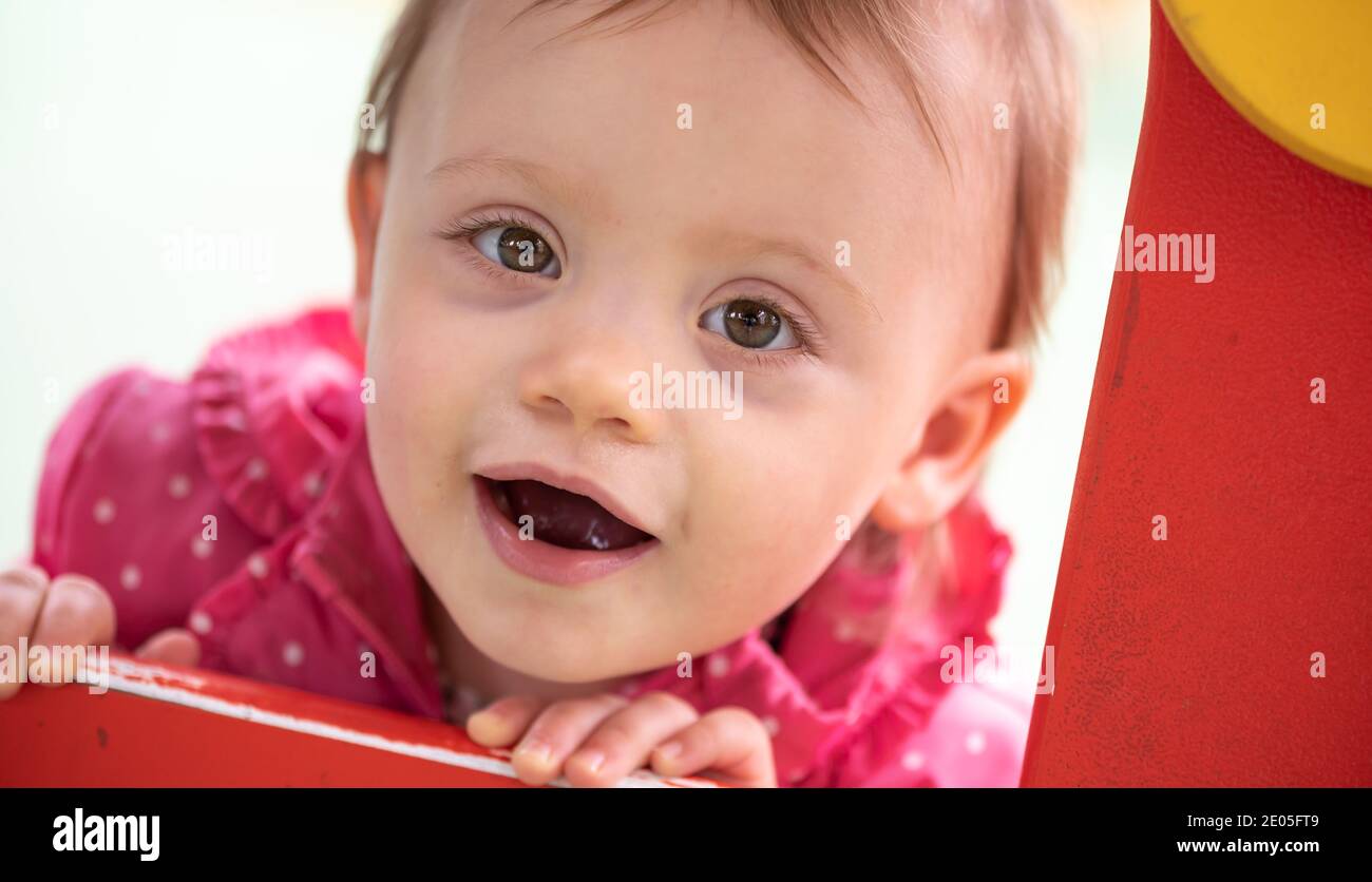 Cute baby girl having fun on a playground and looking at the camera ...
