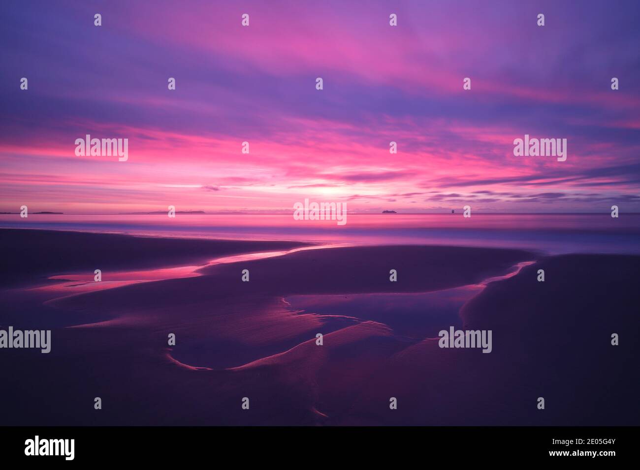 The rising sun fills a winter sky with magical pink colour over tidal ...