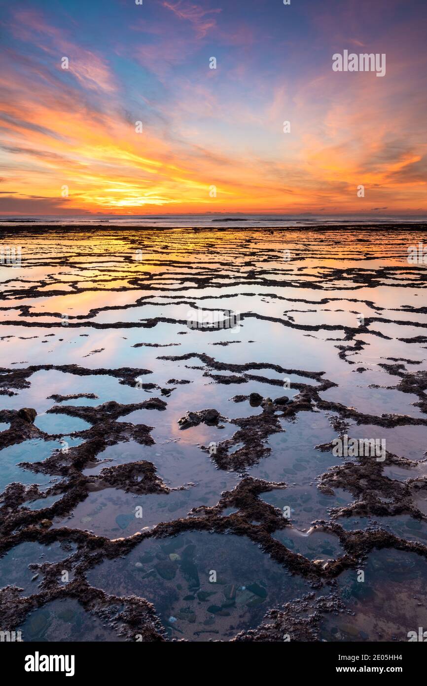 A vertical view of a beautiful sunset over the ocean with rocky beach ...