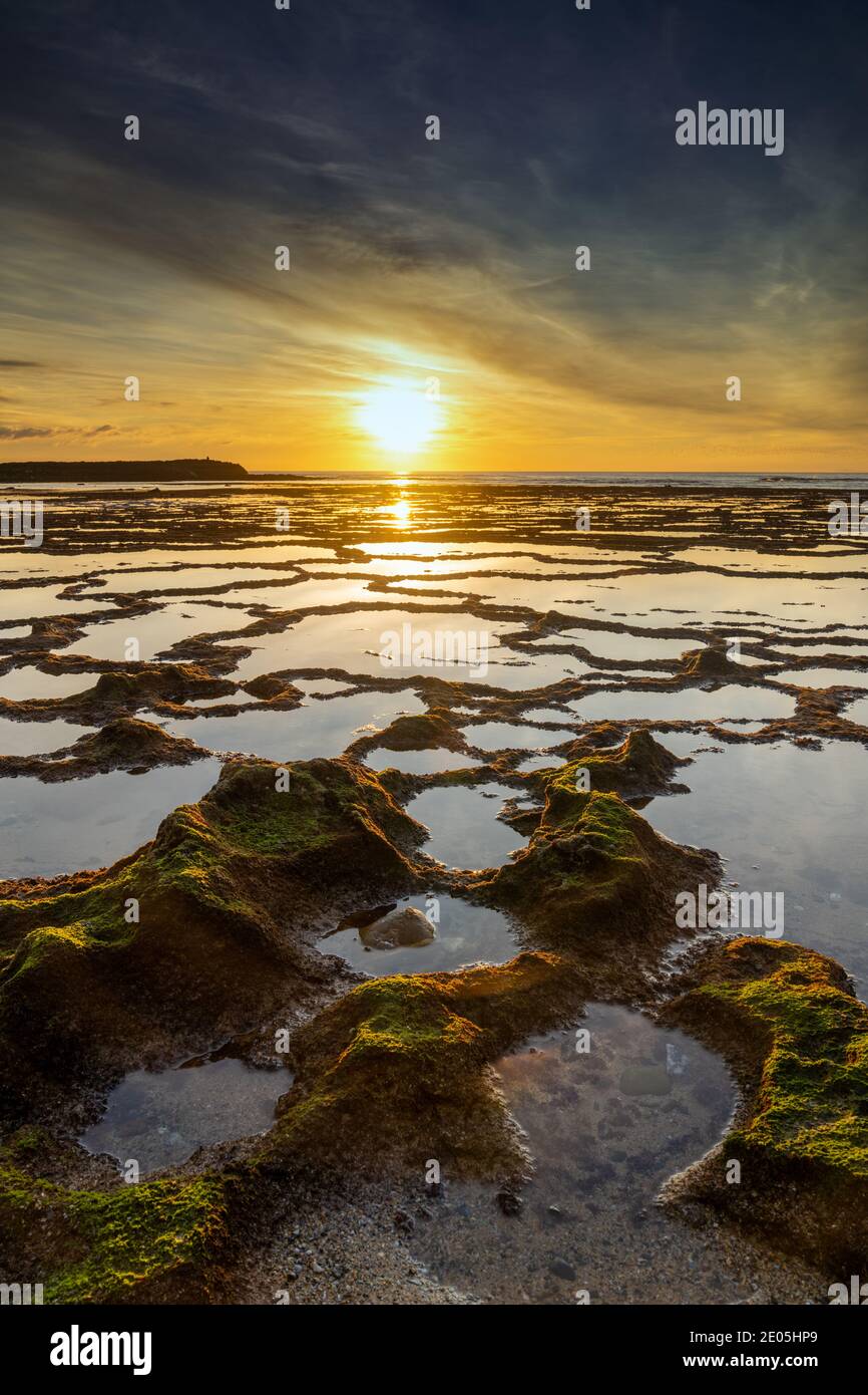 A vertical view of a beautiful sunset over the ocean with rocky beach ...