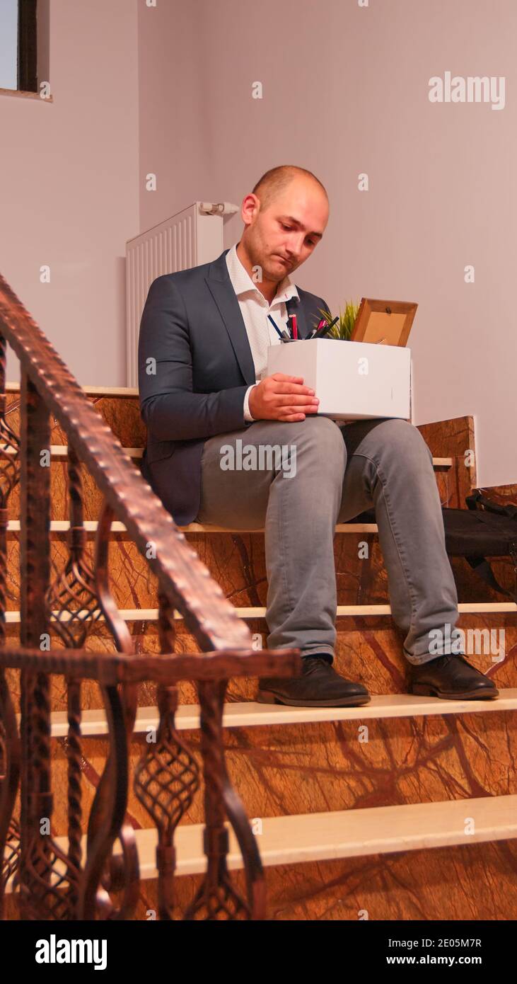 Upset business corporate employee sitting on stairs holding box of ...
