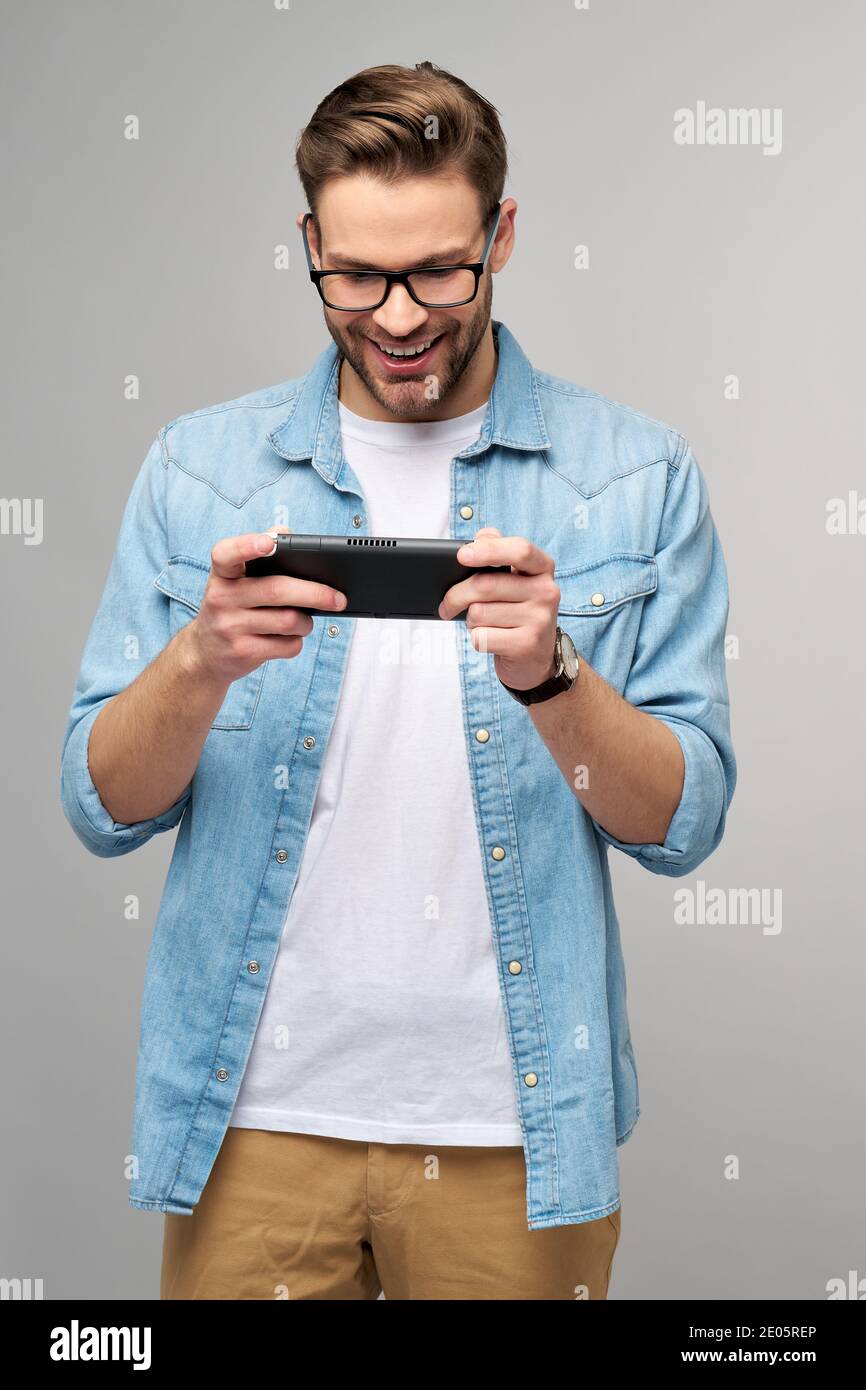 Young handcome man playing with portable video game standing over grey ...