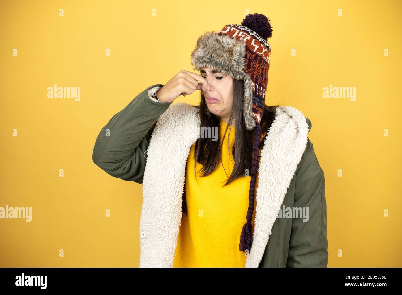 Young beautiful woman wearing a hat and a green winter coat over yellow ...