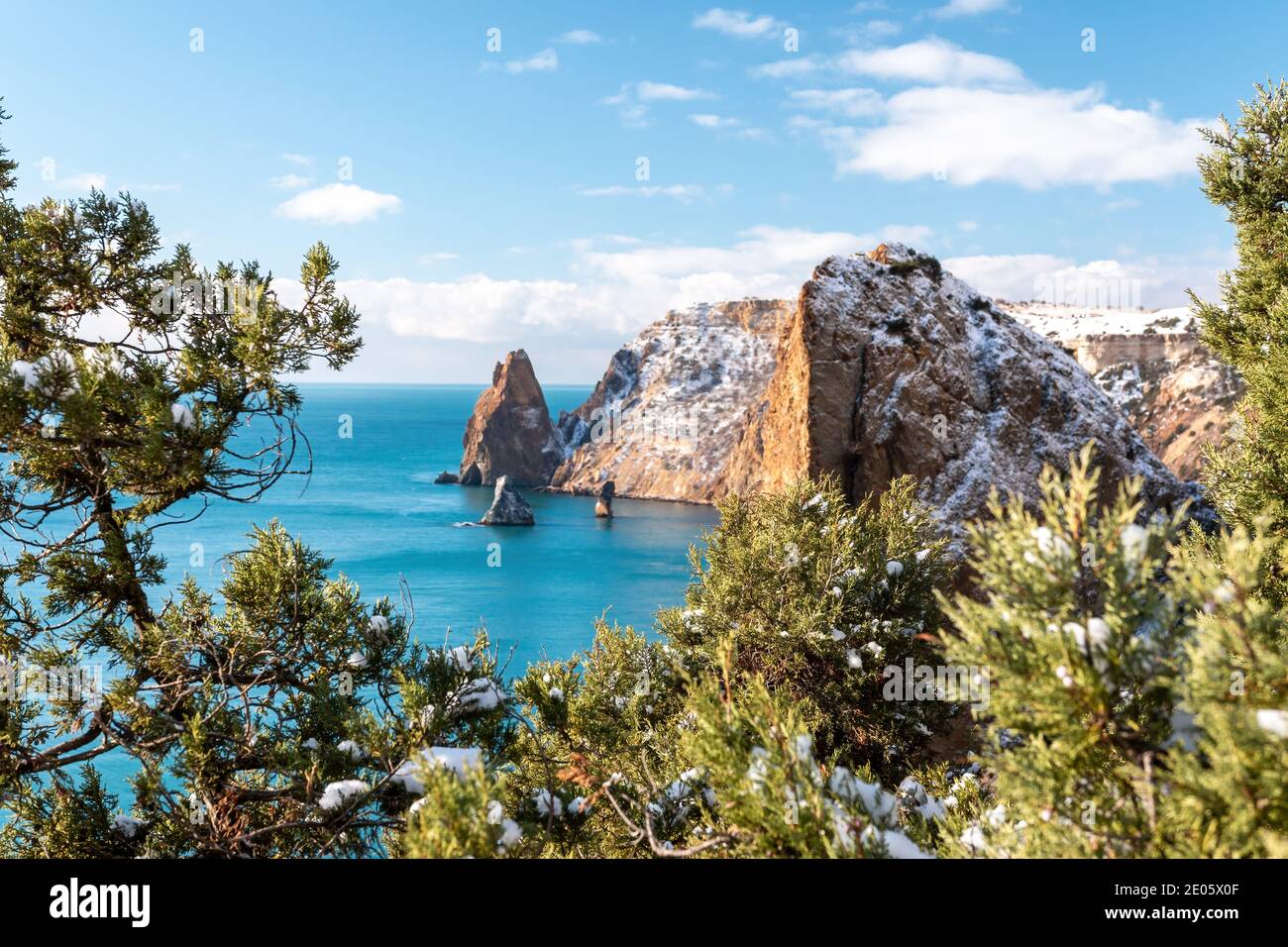 Snow covered rocky cliffs over sea. Winter sunset over the sea bay ...