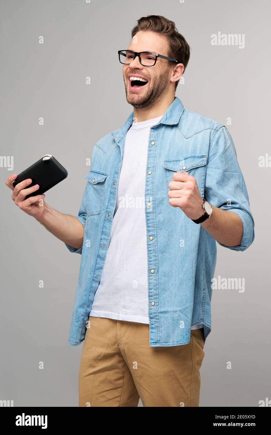 Young handcome man playing with portable video game standing over grey ...