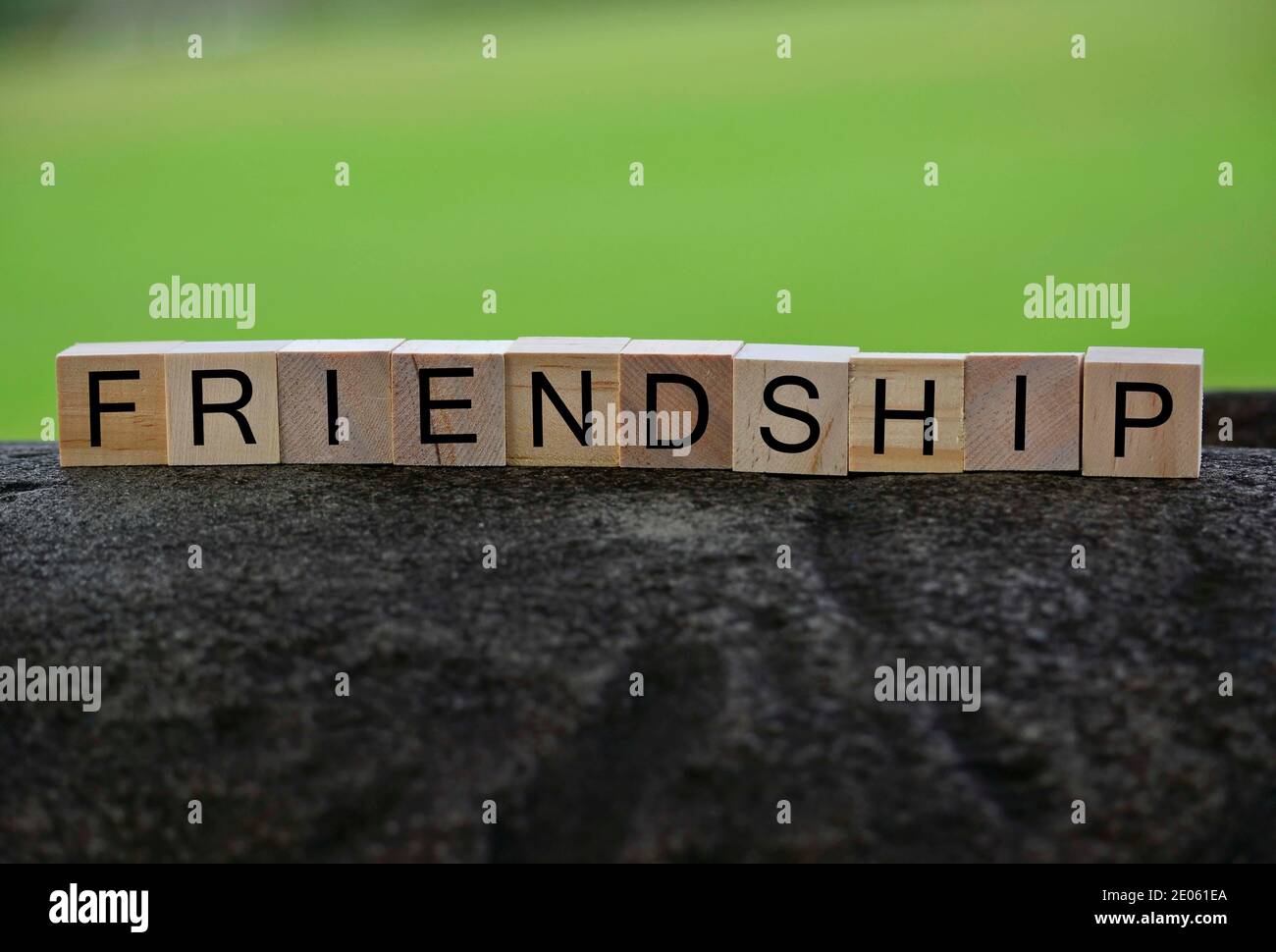 Friendship text on wooden cube block on top of big stone with blurred ...