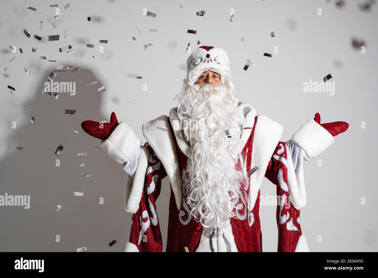 Santa claus under festive xmas confetti showing welcome gesture, studio ...