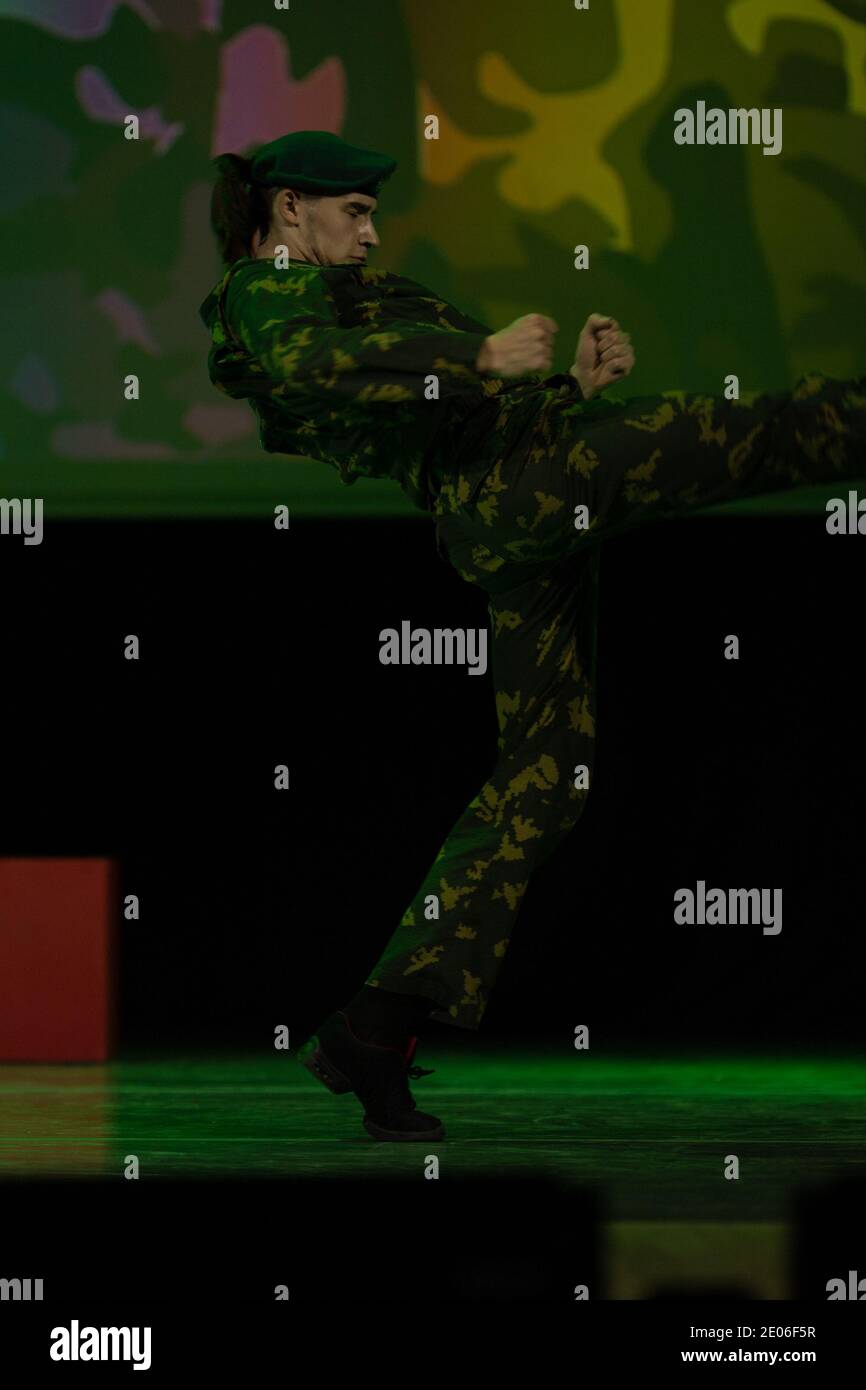 A young guy in military uniform is dancing on stage in a stage light ...
