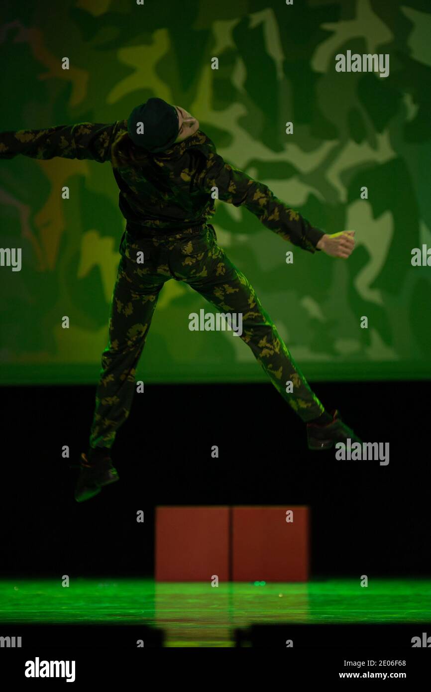A young guy in military uniform is dancing on stage in a stage light ...