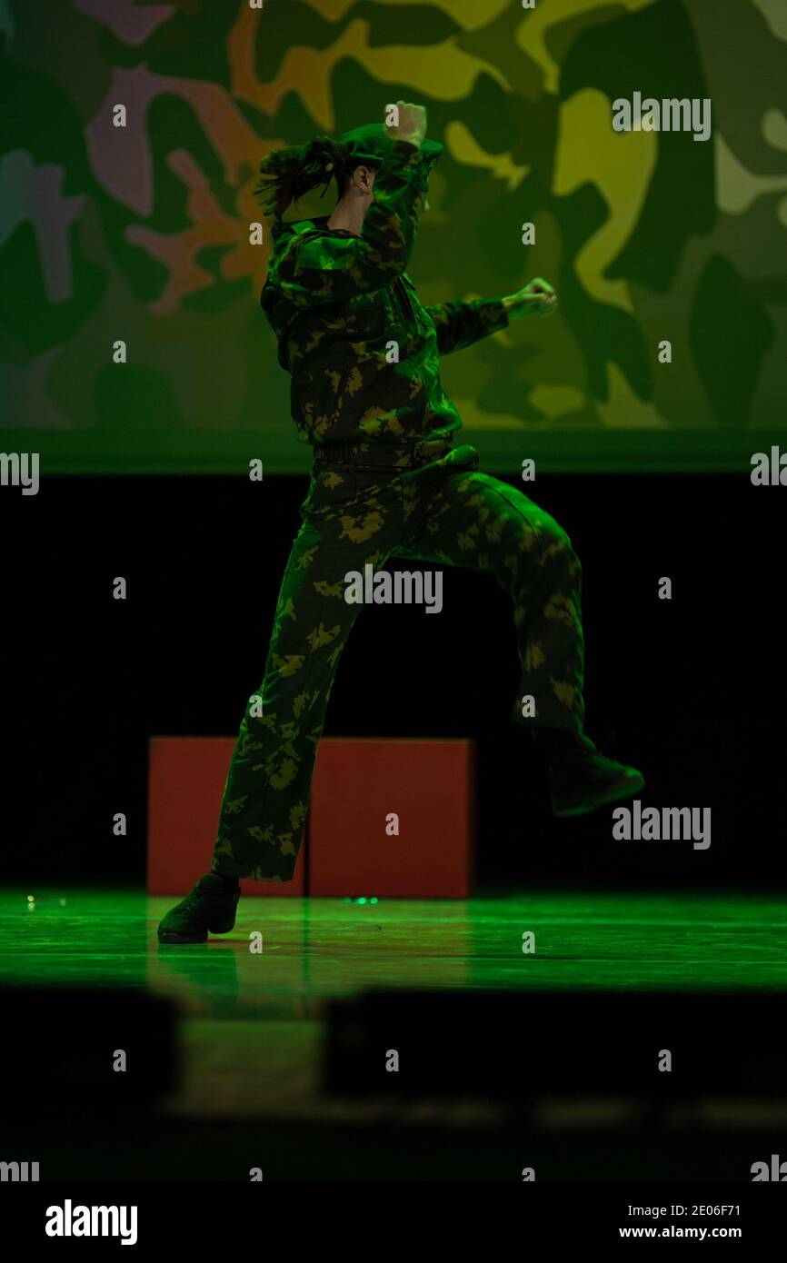 A young guy in military uniform is dancing on stage in a stage light ...