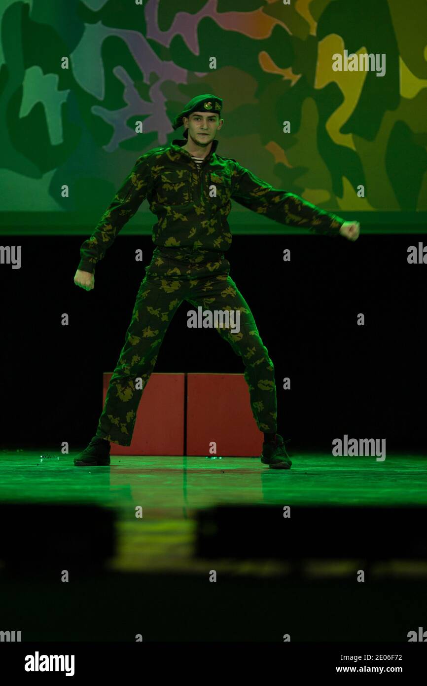 A young guy in military uniform is dancing on stage in a stage light ...