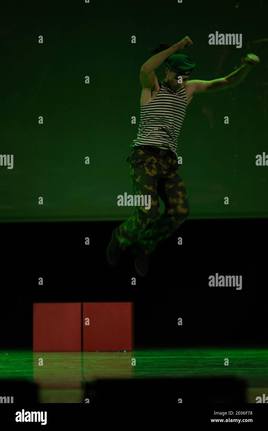 A young guy in military uniform is dancing on stage in a stage light ...