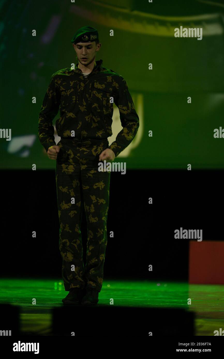 A young guy in military uniform is dancing on stage in a stage light ...
