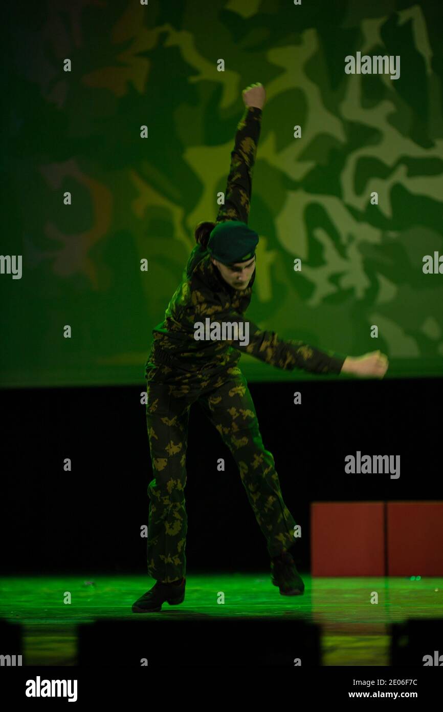 A young guy in military uniform is dancing on stage in a stage light ...