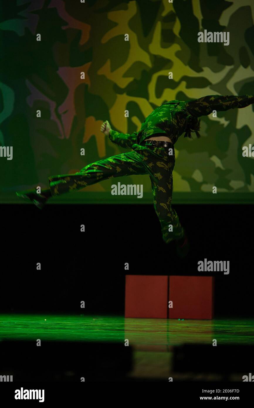 A young guy in military uniform is dancing on stage in a stage light ...