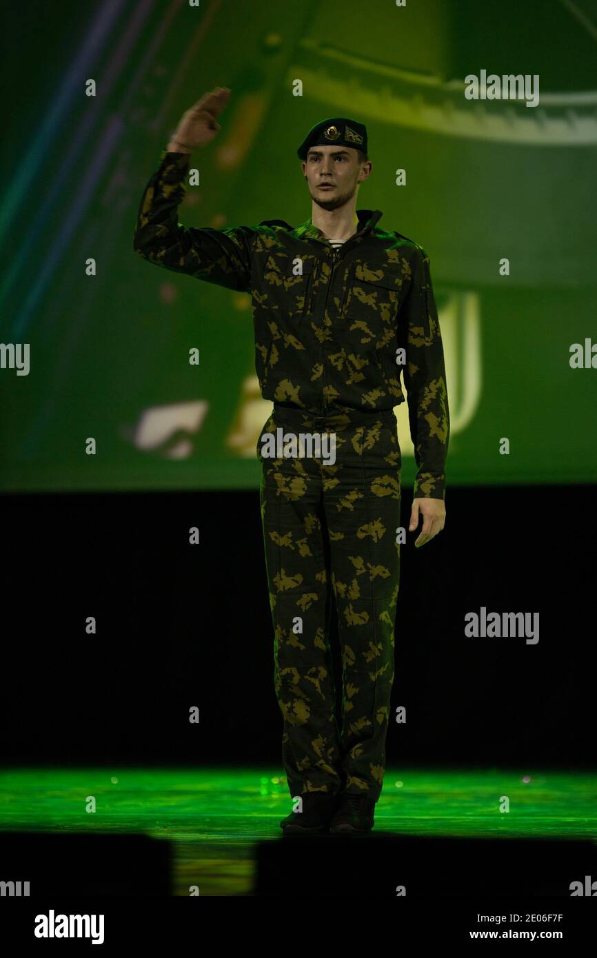 A young guy in military uniform is dancing on stage in a stage light ...