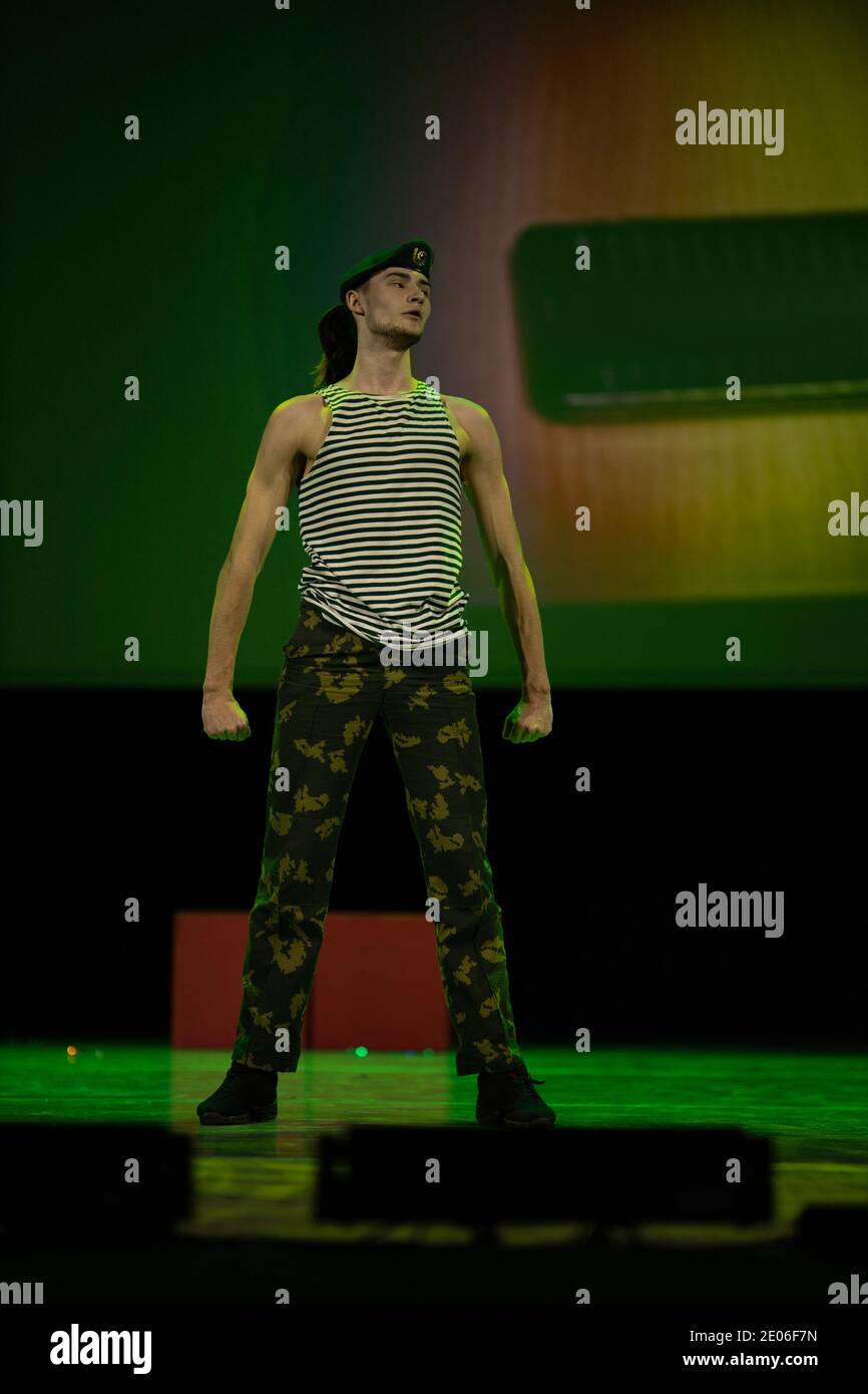 A young guy in military uniform is dancing on stage in a stage light ...