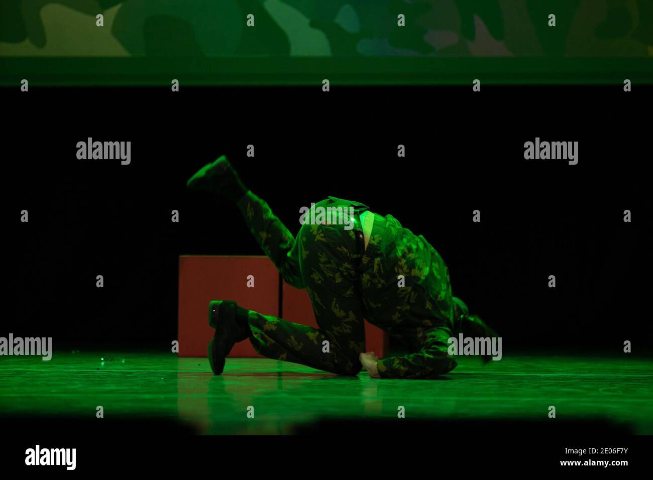 A young guy in military uniform is dancing on stage in a stage light ...