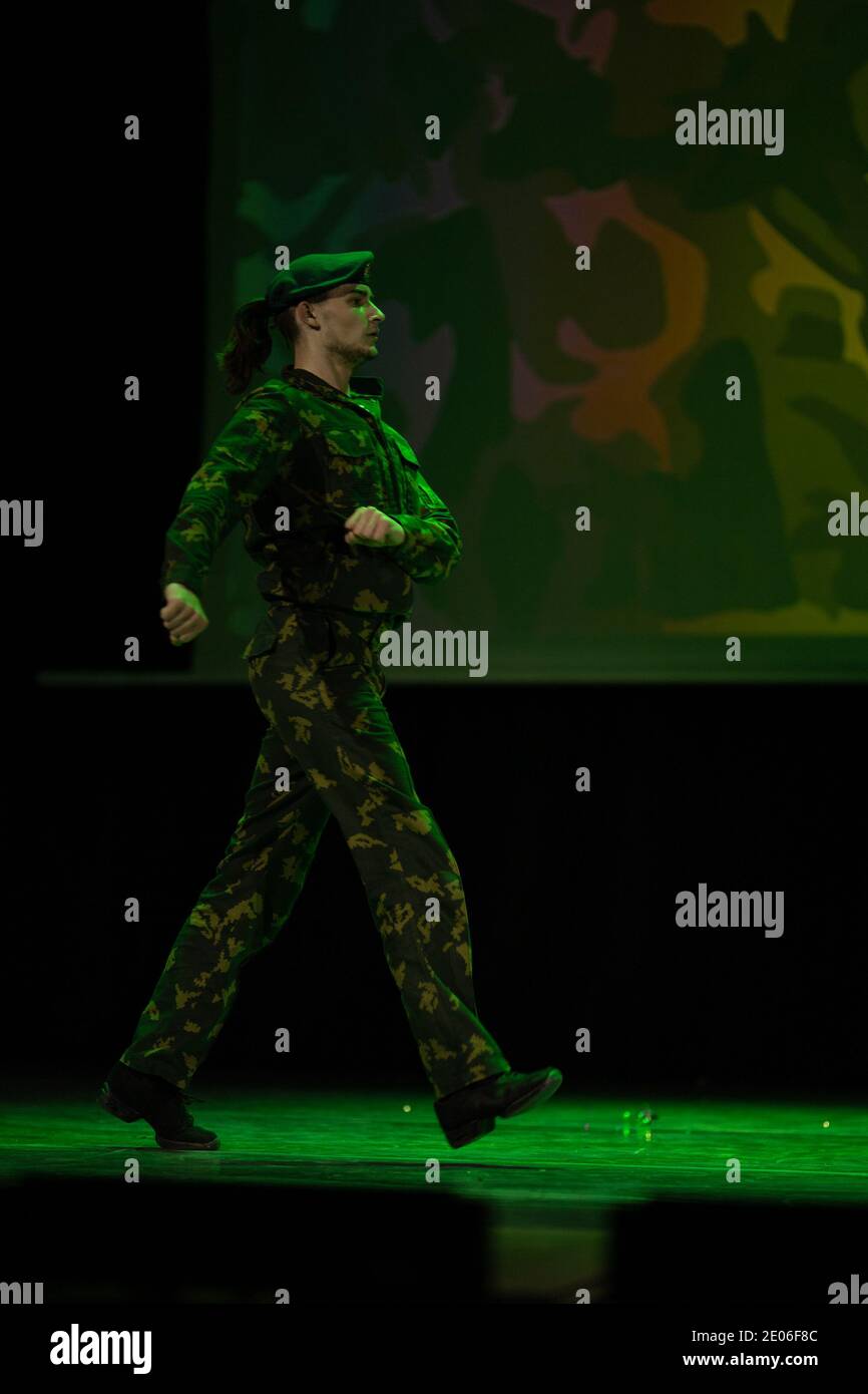 A young guy in military uniform is dancing on stage in a stage light ...