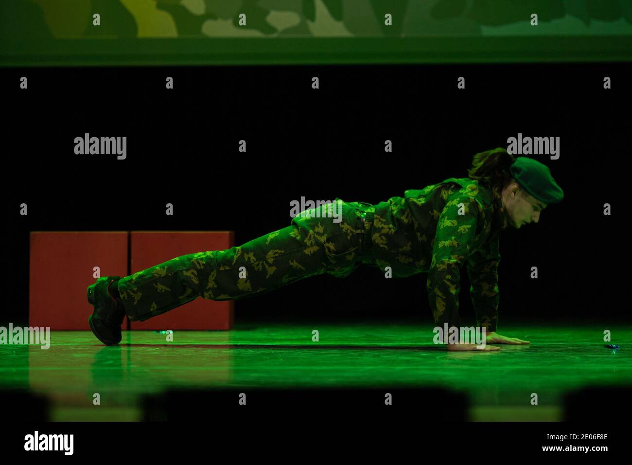 A young guy in military uniform is dancing on stage in a stage light ...