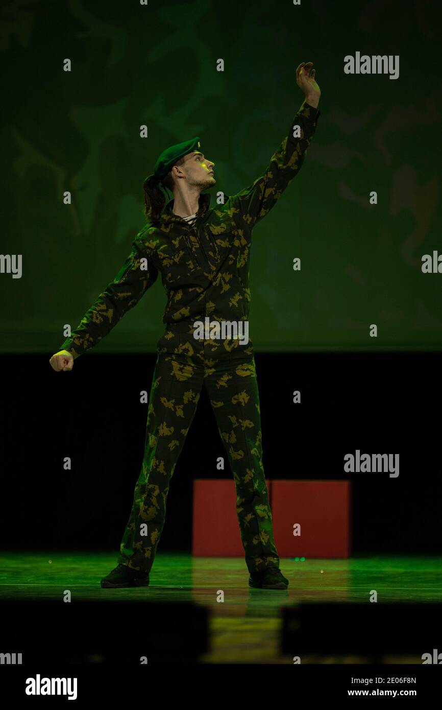 A young guy in military uniform is dancing on stage in a stage light ...