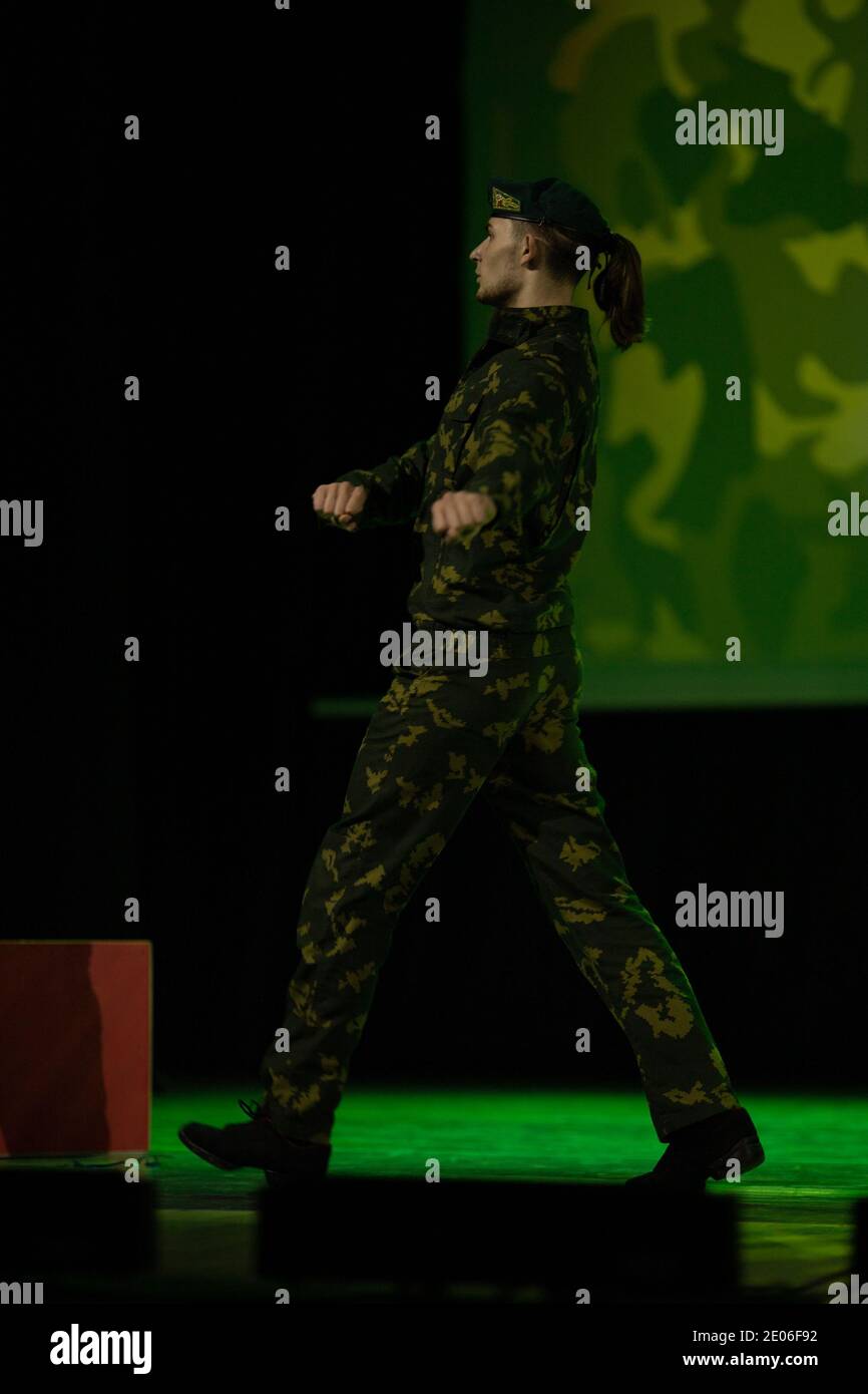 A young guy in military uniform is dancing on stage in a stage light ...