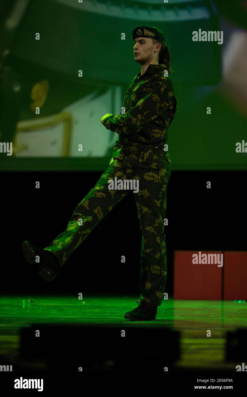 A young guy in military uniform is dancing on stage in a stage light ...