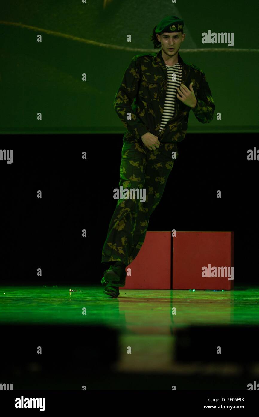 A young guy in military uniform is dancing on stage in a stage light ...