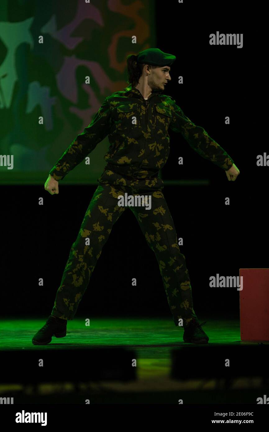 A young guy in military uniform is dancing on stage in a stage light ...