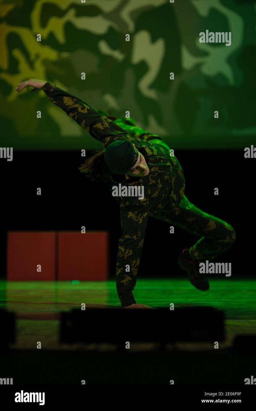 A young guy in military uniform is dancing on stage in a stage light ...