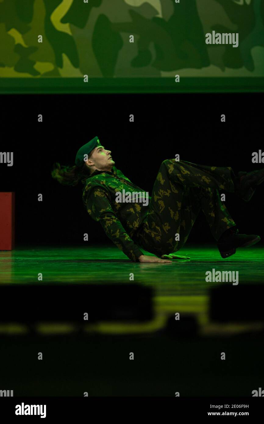 A young guy in military uniform is dancing on stage in a stage light ...