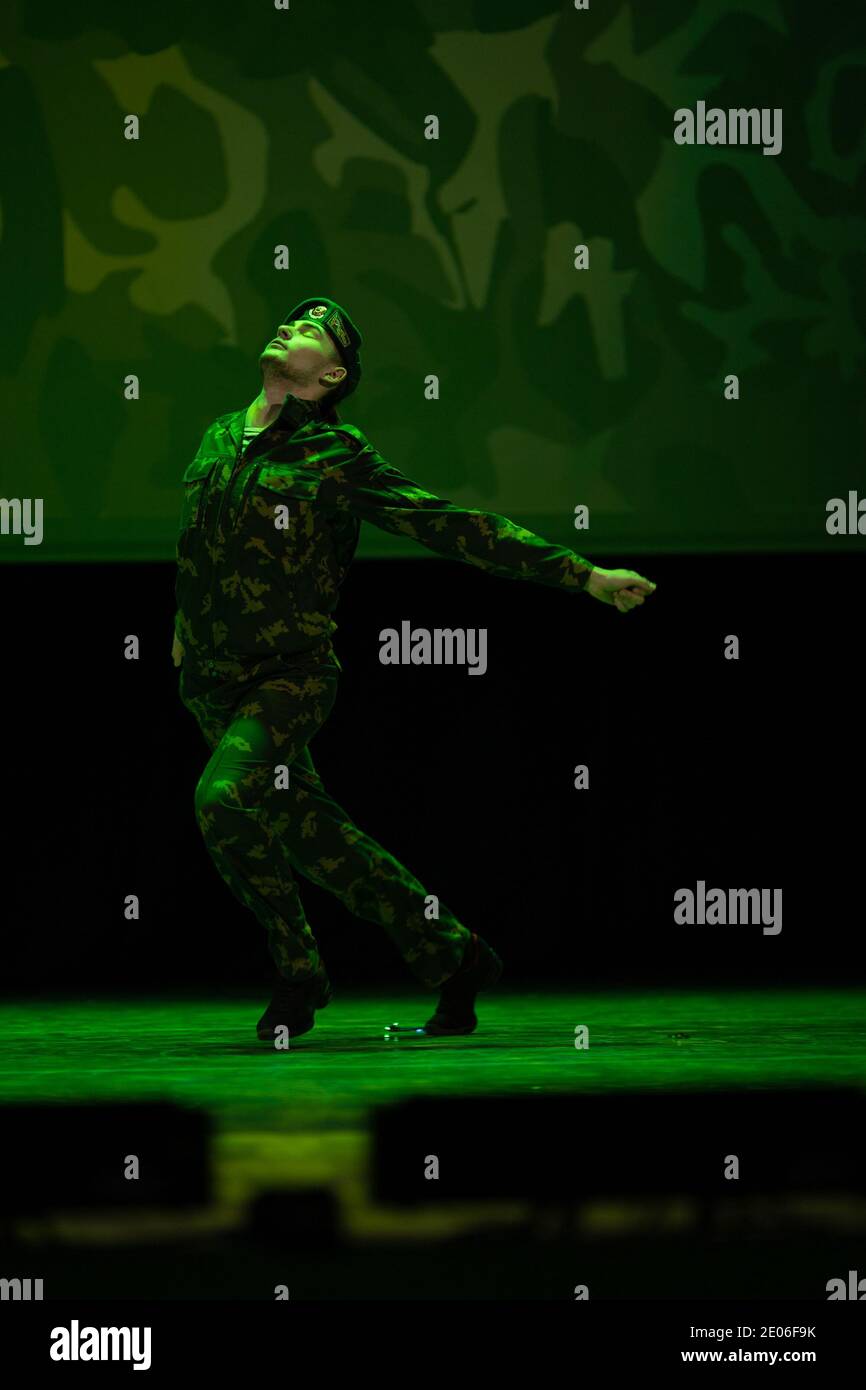 A young guy in military uniform is dancing on stage in a stage light ...
