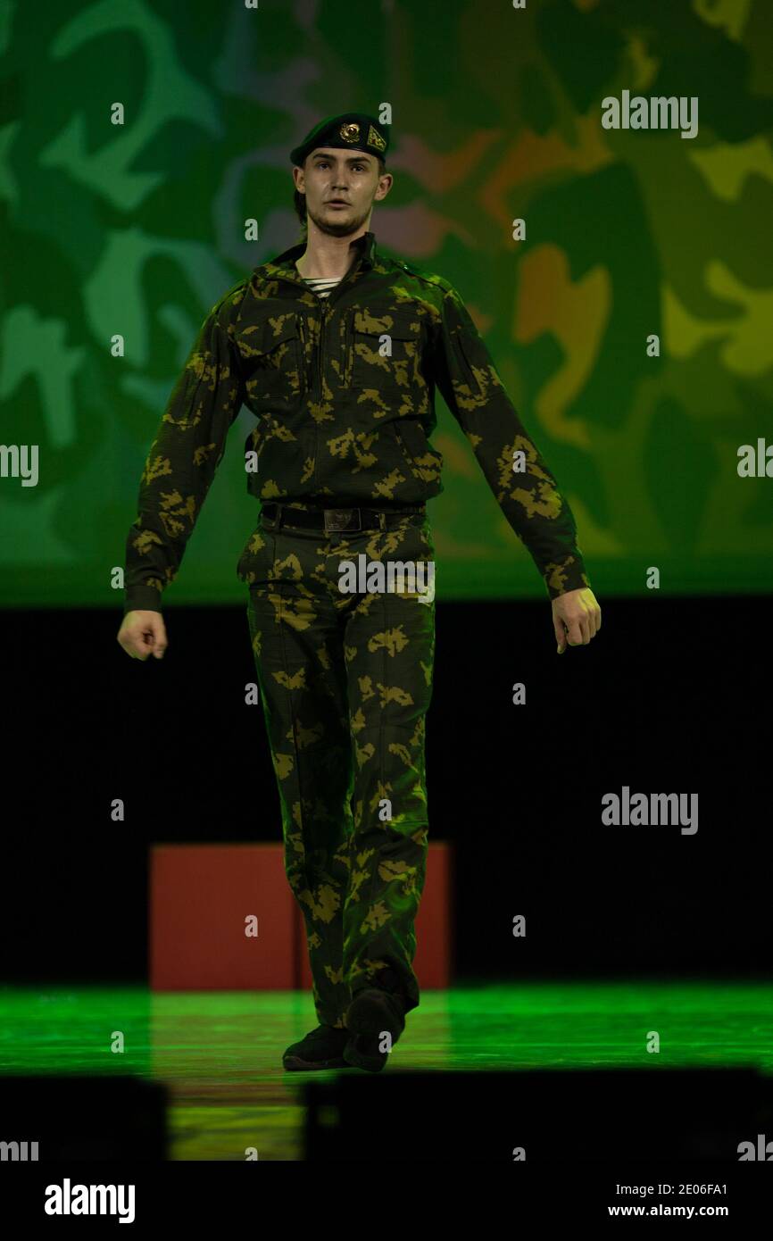 A young guy in military uniform is dancing on stage in a stage light ...